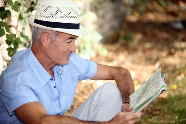 65 years old man sitting in the grass and watching a book - Stock Image ...